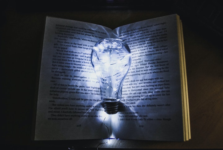 A shining light bulb placed in the middle of a book represents creative ...